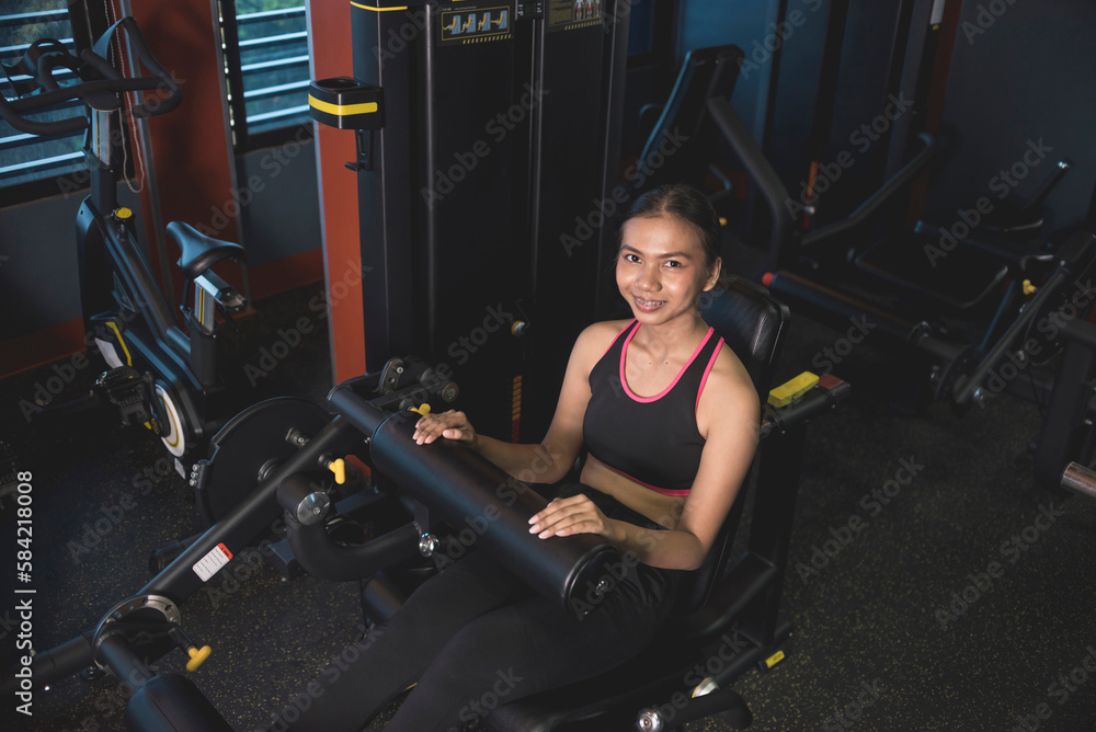 A young asian woman does leg extensions. Looking at camera while using ...