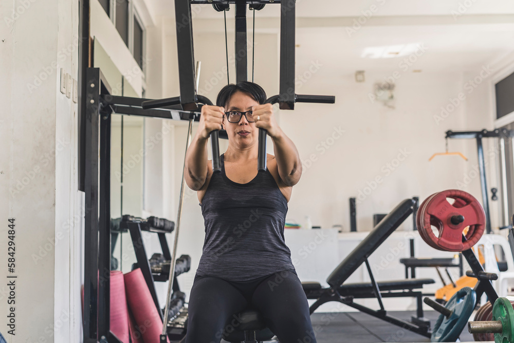 A short haired asian woman does a set of chest flys on a pec deck ...