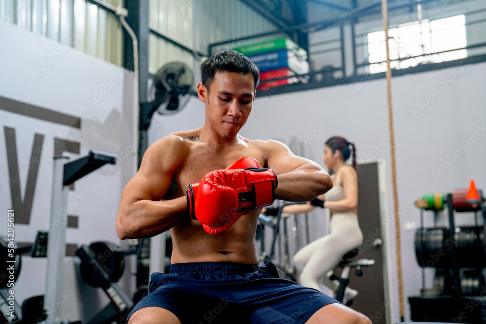 Asian sport man sit on chair and try to wear boxing glove in front of ...