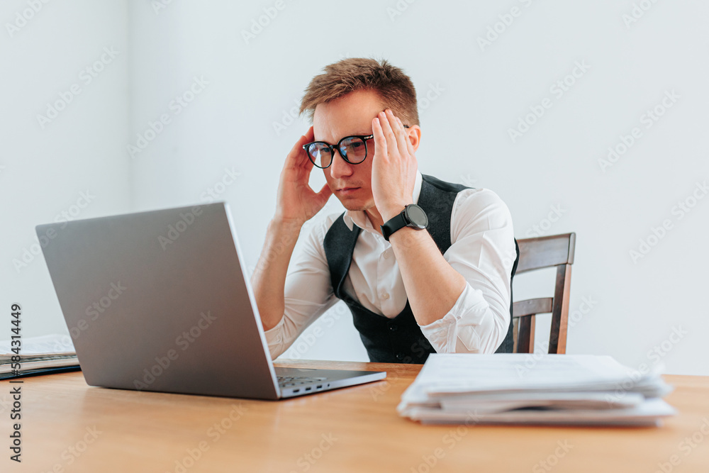 A guy in eyeglasses looks exhausted and overwhelmed as he works at his ...