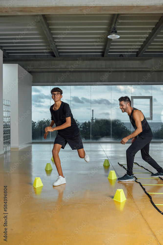 Full length of personal trainer encouraging boy during circuit training ...