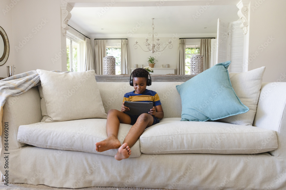 Happy african american boy sitting on sofa, wearing headphones and ...