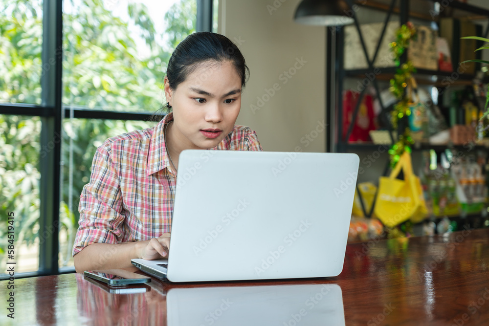 Cheerful young Asian woman using laptop while sitting on chair alone at ...