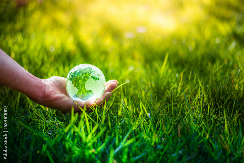 Hand holding glass Earth globe in green grass. Earth Day environment ...