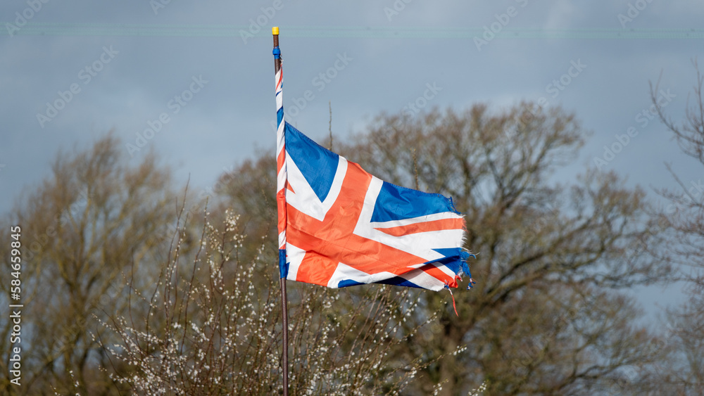 Ragged and torn British union flag flying from metal pole in front of ...