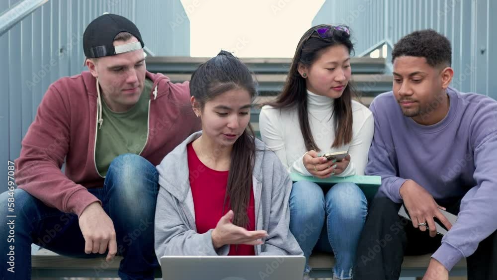 Young multiracial college students sitting on staircase at campus university using laptop ...