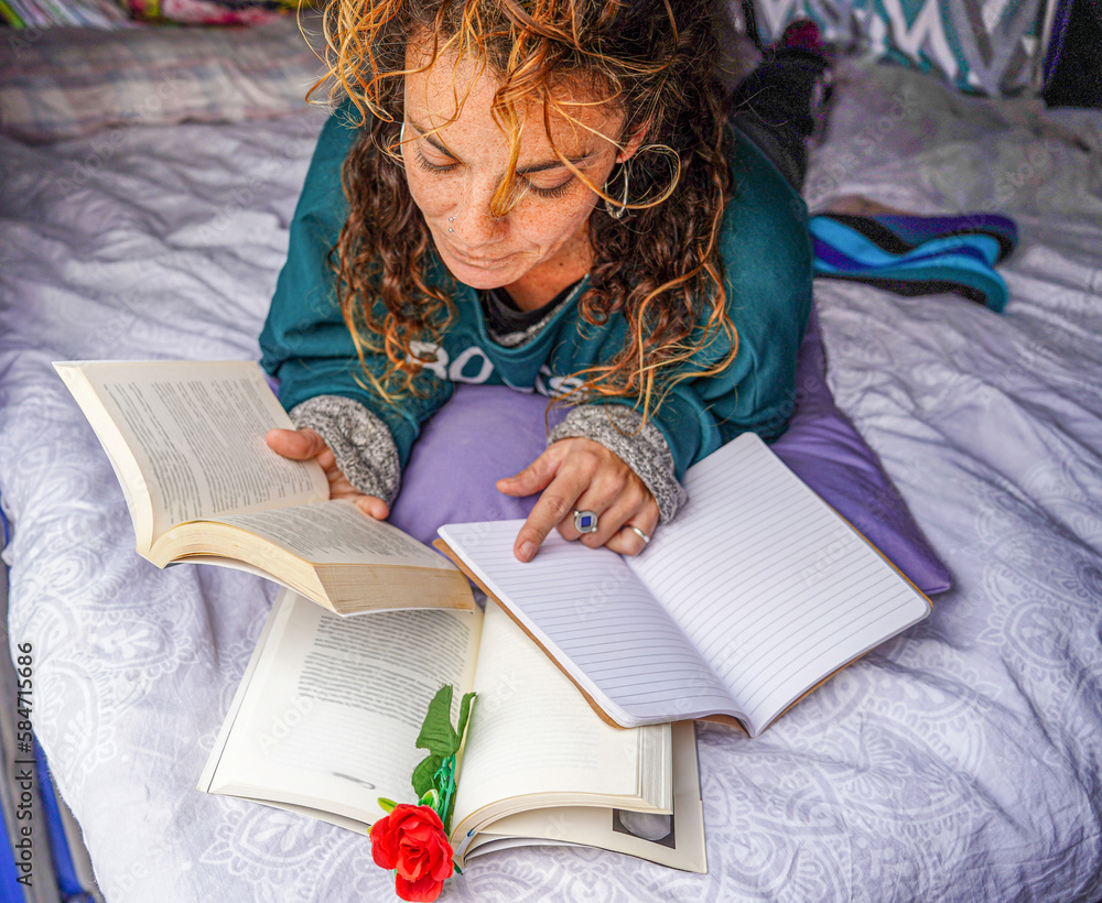 concentrated woman lying in bed reading many books with a rose. World ...