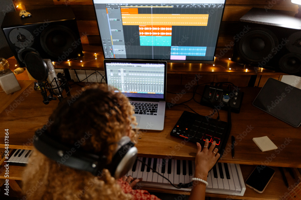 Music producer at home studio using keyboard controller from behind ...