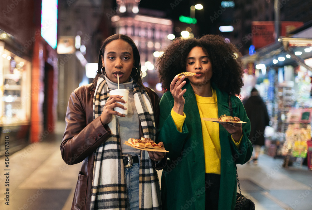 Foto de Young black women eating fast food on the street at night do ...