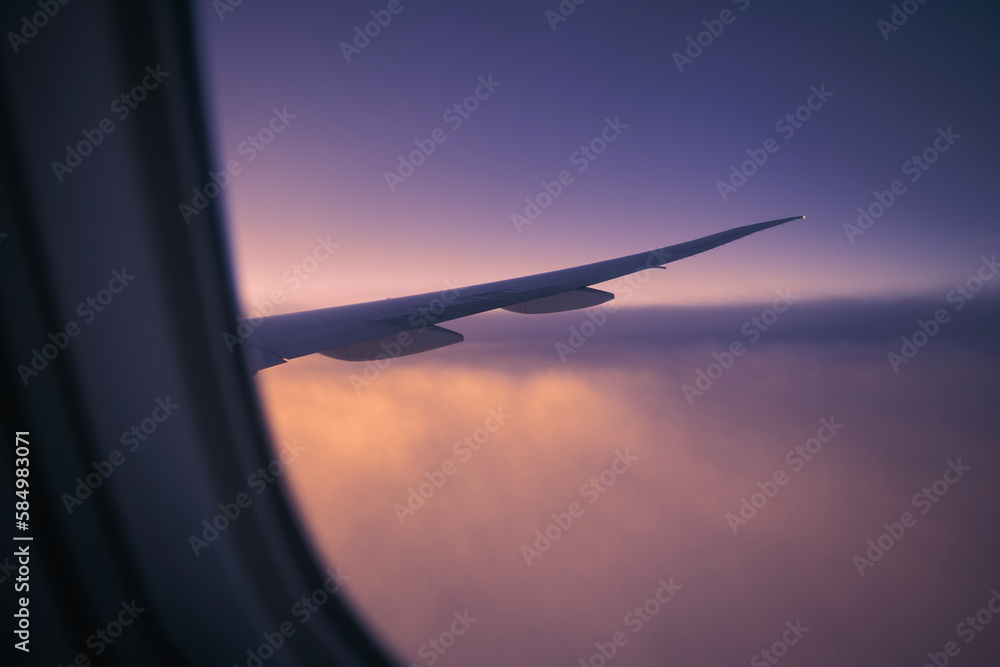 View from window of airplane during flight above clouds at dawn. Selective focus on aircraft ...