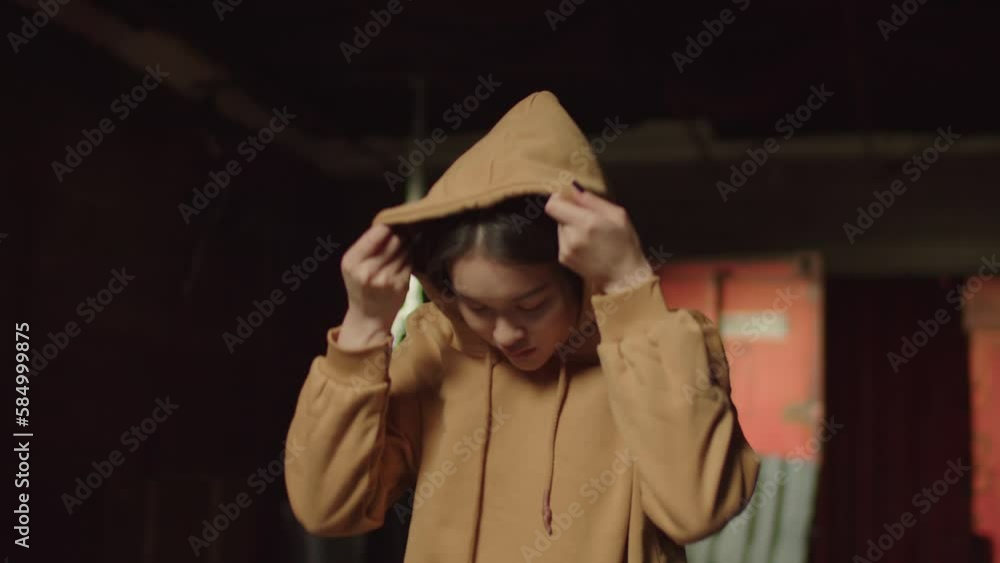Cool street gang style attractive Asian young woman putting on hoodie ...