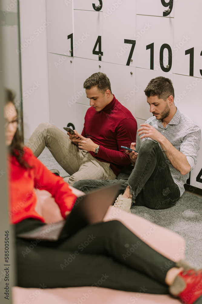 Two tired male coworkers playing games on their phones while sitting on ...