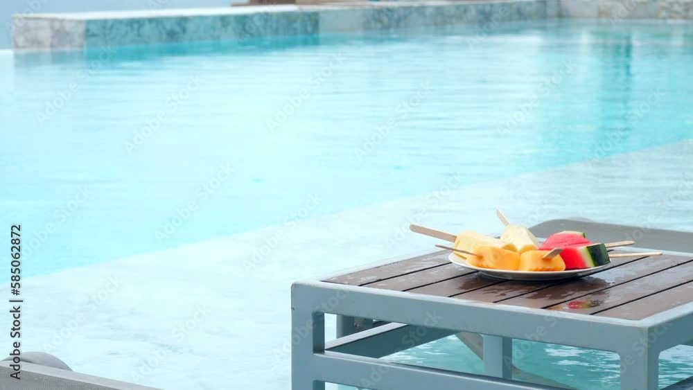 Table with tropical fruits plate on sticks in swimming pool in modern ...