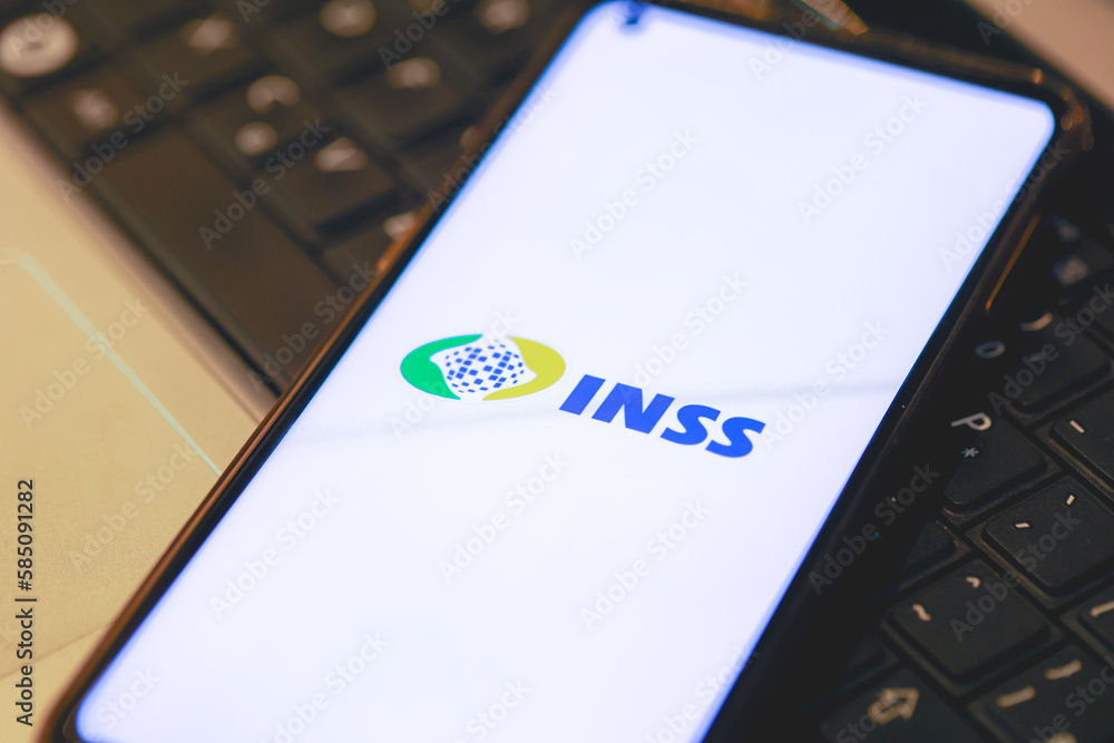 A logo do INSS na tela de um telefone celular que está sobre um teclado ...