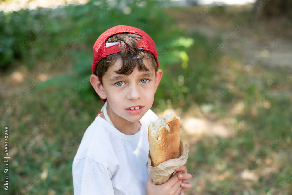 A young boy eats a loaf of bread on street, the boy is hungry and very ...