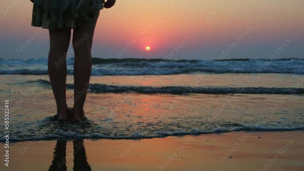 Romantic barefoot woman standing on the beach at sunset. Low section ...