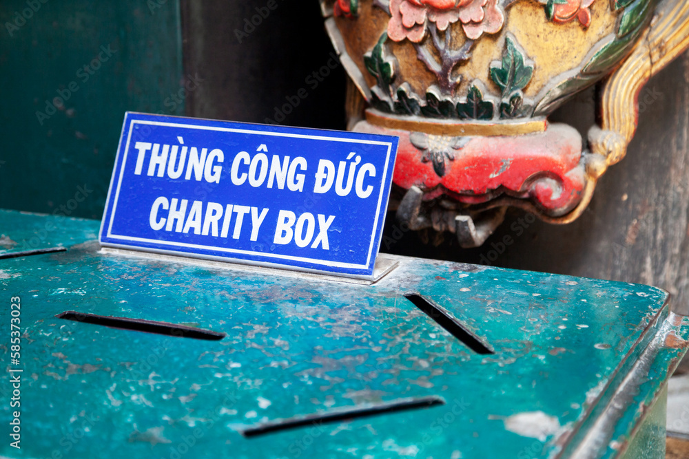 Green donation box with a sign in Vietnamese and English in a temple. A ...