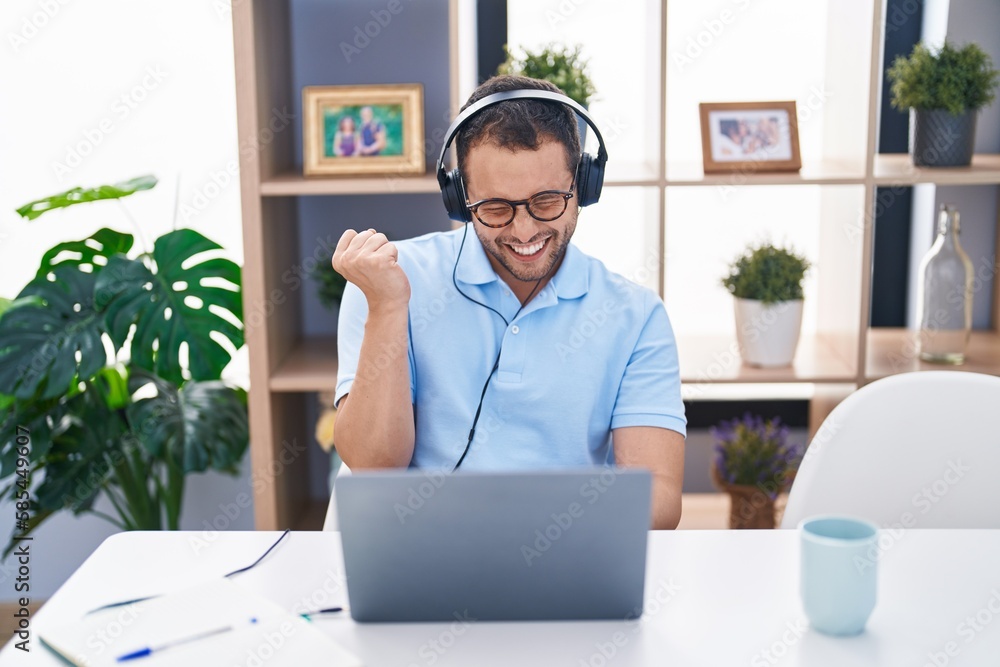 Hispanic man working using computer laptop wearing headphones screaming ...