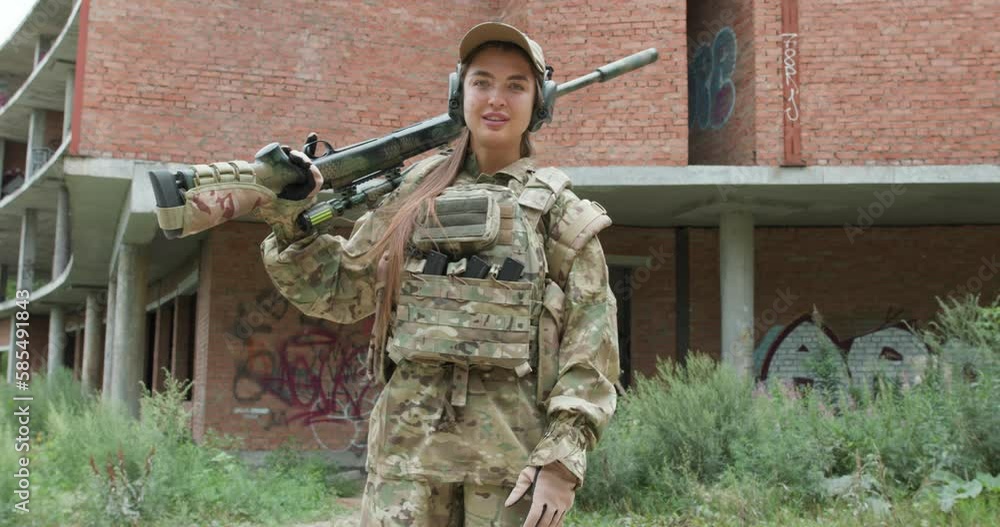 positive young woman with rifle on her shoulder is posing to camera ...