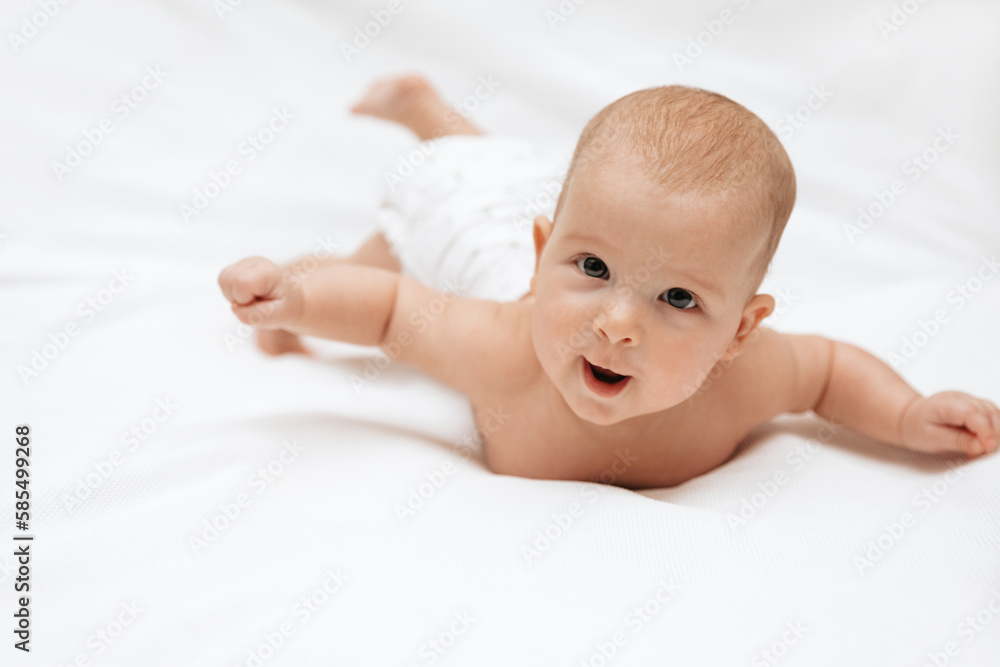 A newborn baby is lying on his stomach and raising arms up like a plane ...