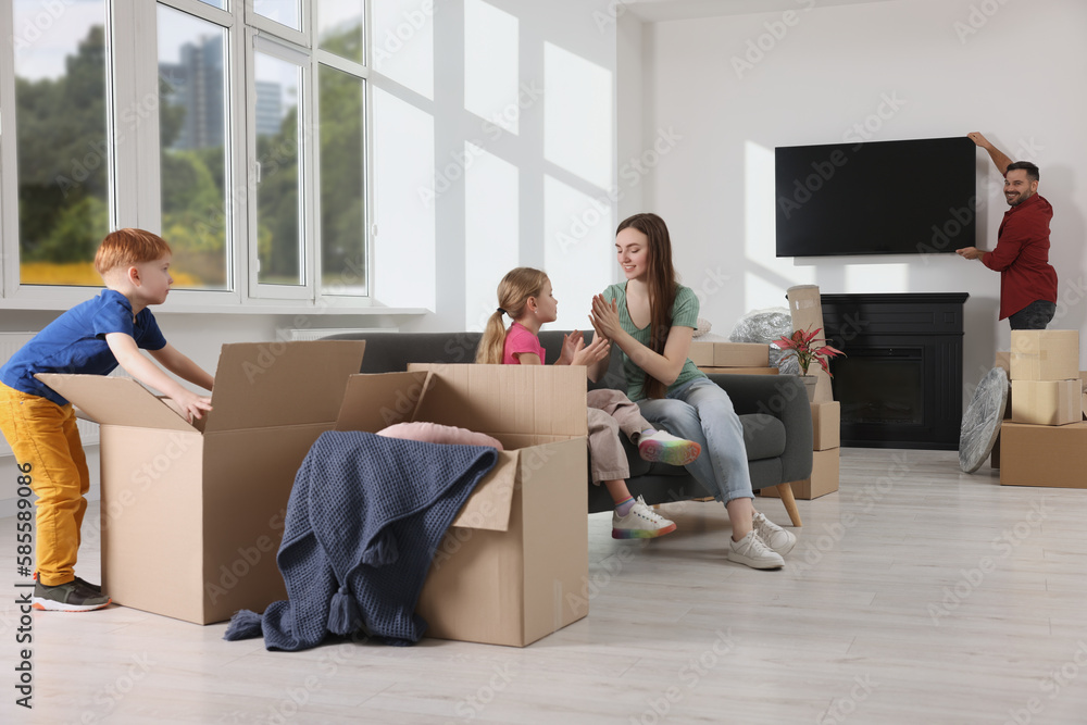 Family settling into new home. Dad setting up TV, happy mom and ... Family settling into new home. Dad setting up TV, happy mom and ...