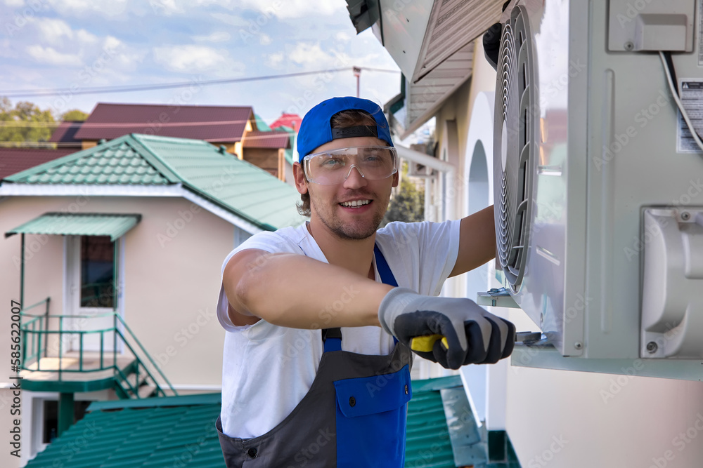 Against background residential buildings, smiling master installs air ...