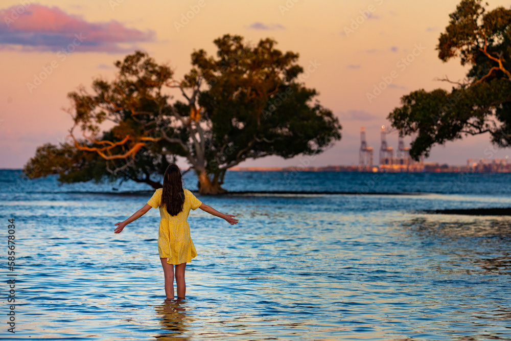 girl in dress admires the amazing colourful sunset wading in the ...
