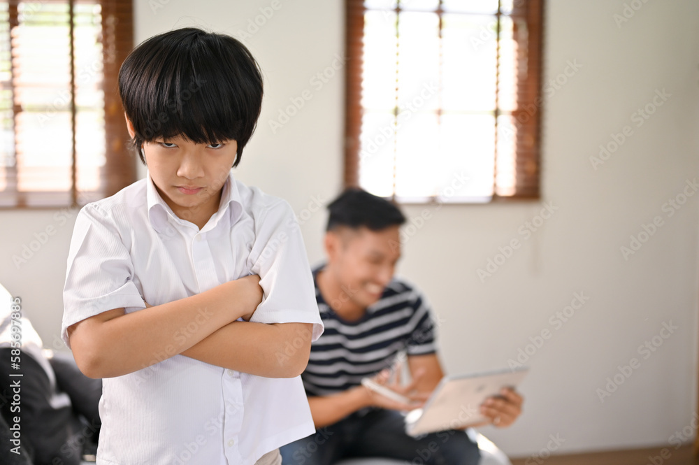 Fotka „An angry young Asian boy stands with his arms crossed, feeling ...