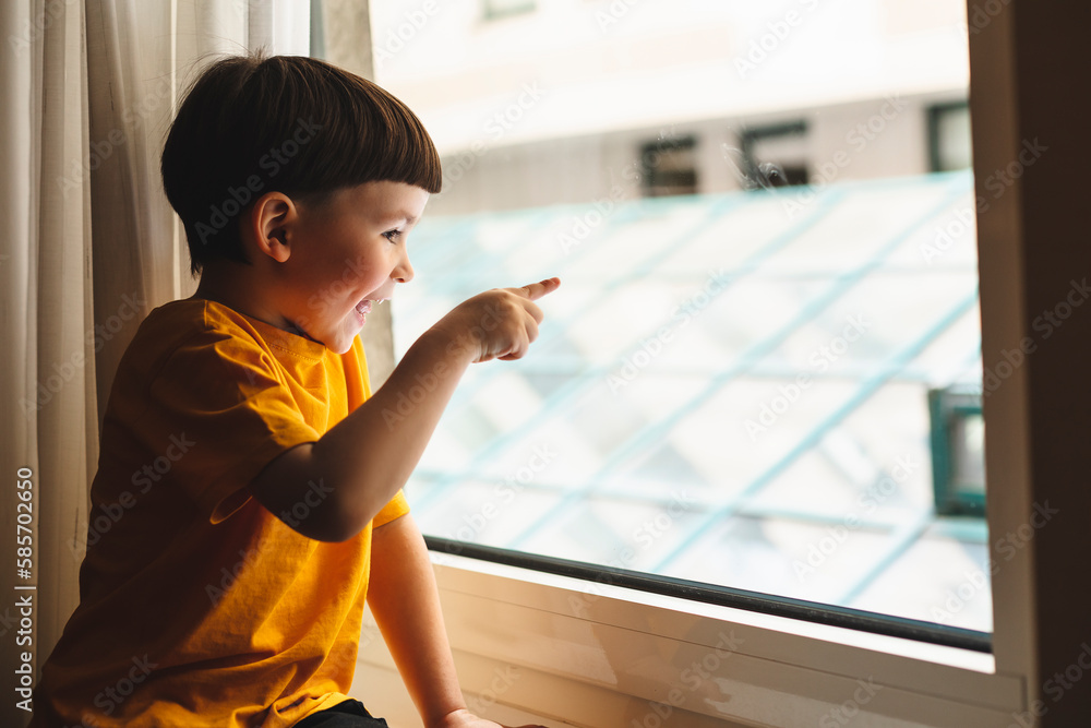 Little cute attractive boy sitting on windowsill and look at window ...