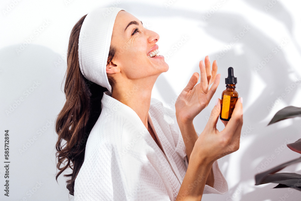 Laughing woman in a white bathrobe takes care of her skin and ...