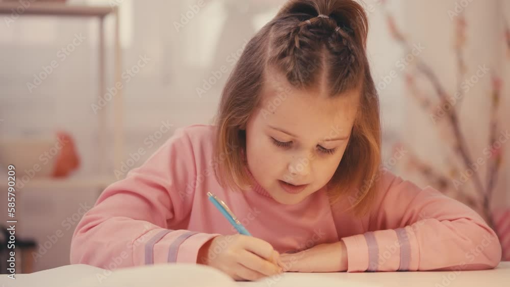 Diligent little girl doing homework and writing in notebook, education ...