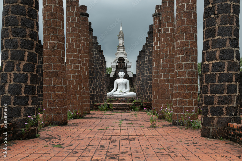 A white stone statue of a seated Buddha stands on a towering brick ...