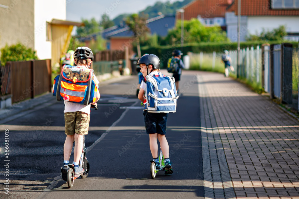 Two school kid boys in safety helmet riding with scooter in the city ...