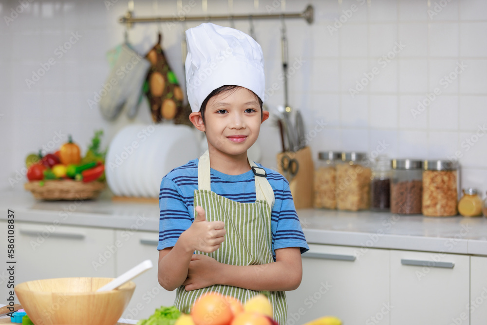 Millennial Asian little boy chef wearing tall white cook hat and apron ...