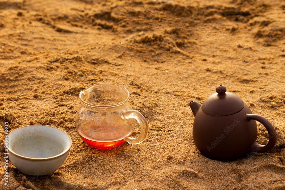 brown earthenware teapot, tea cup and glass teapot on a sandy beach ...