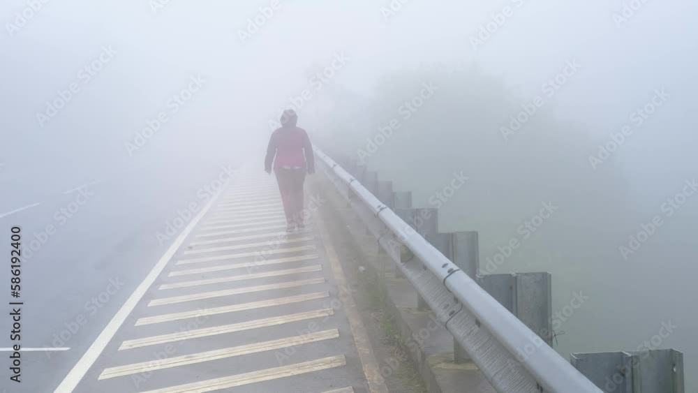 woman in burgundy hooded jacket runs in thick fog along road out focus ...