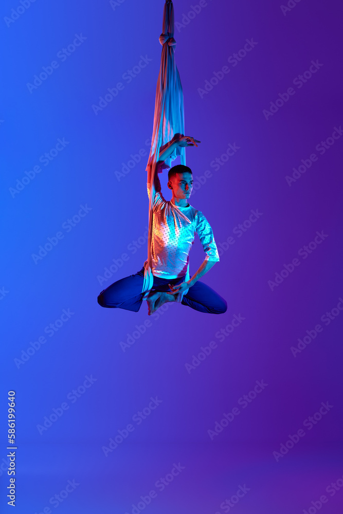 Male acrobat, professional, artistic aerial gymnast hanging upside down ...