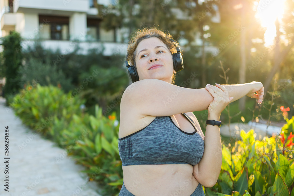 Adorable fat woman in tracksuit is engaged in fitness outdoor side view ...