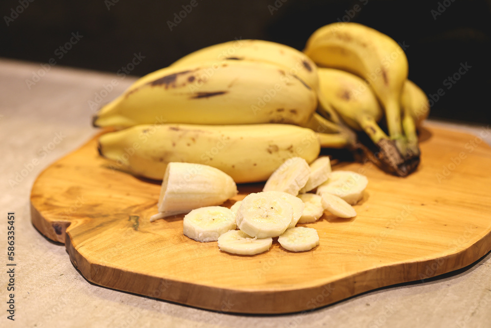 Banana picada com cacho de banana ao fundo sobre uma tábua de madeira ...