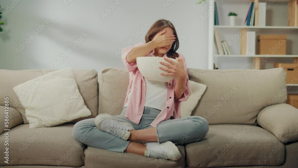 A Young Woman Sitting on the Sofa, Eating Popcorn and Watching a Scary ...
