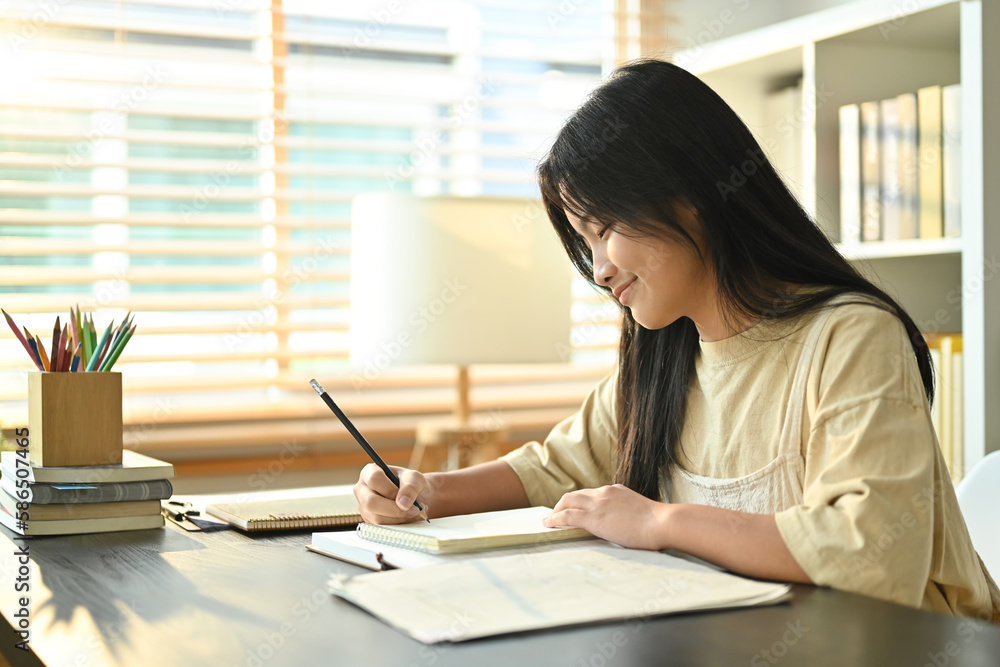 Image of smiling asian teenage student, doing homework, writing task ...