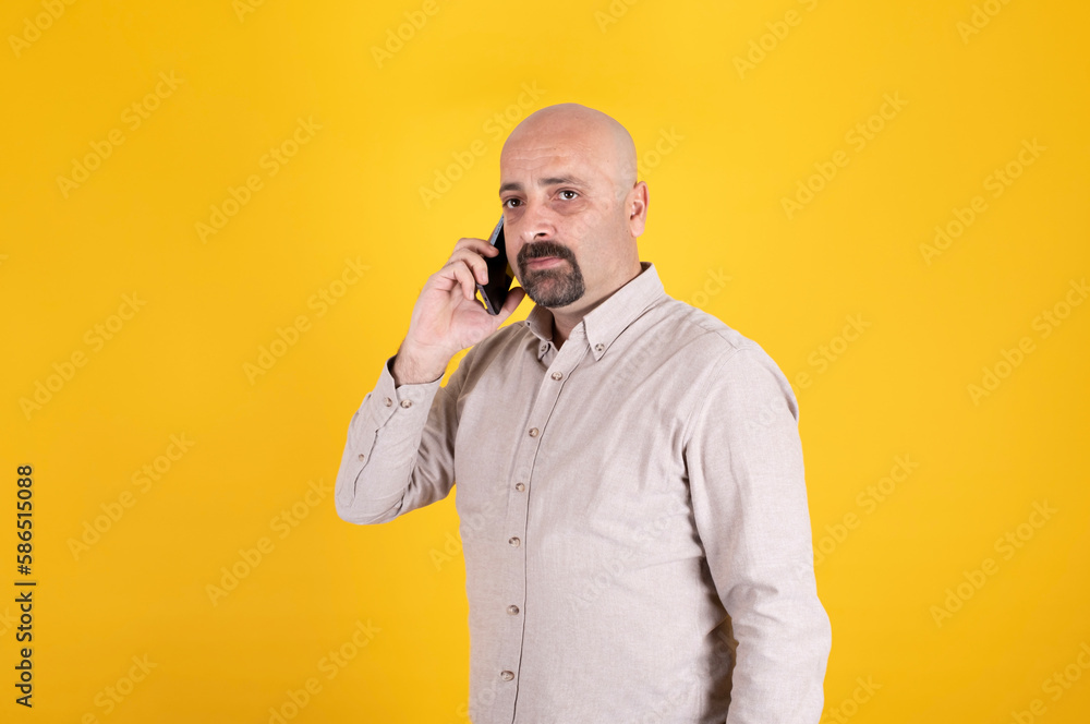 Middle aged man talking on the phone, standing over yellow studio ...