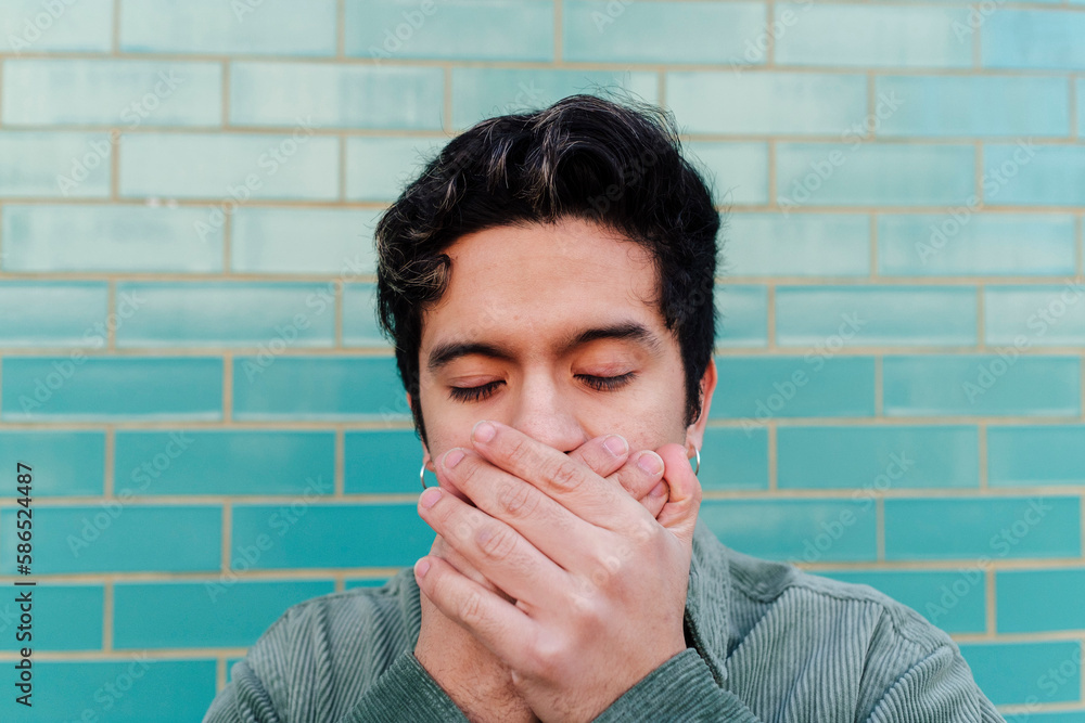 Young man covering mouth with hands in front of brick wall Stock Photo ...