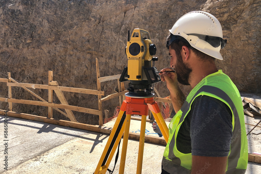 Land surveyor stands by theodolite on a tripod against construction ...