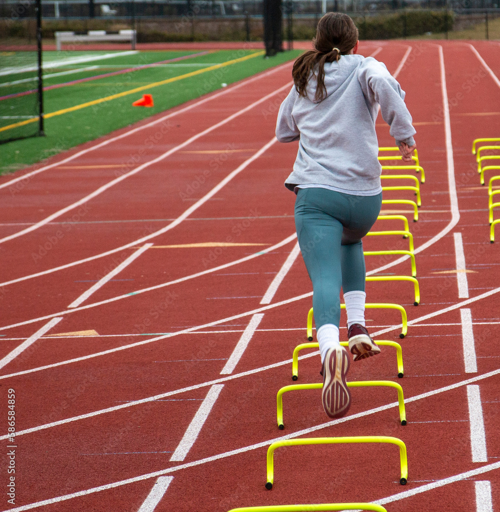 Rear view of female runner wearing spandex running over six inch mini hurdles on a track Stock ...