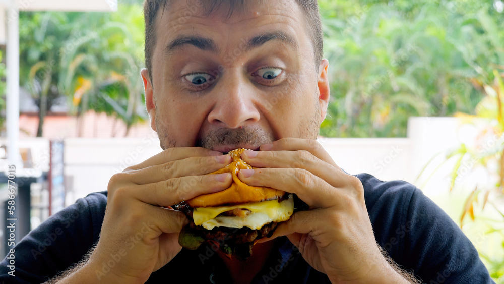 Foto de Man eat juicy hamburger at an outdoor restaurant. Man enjoys ...