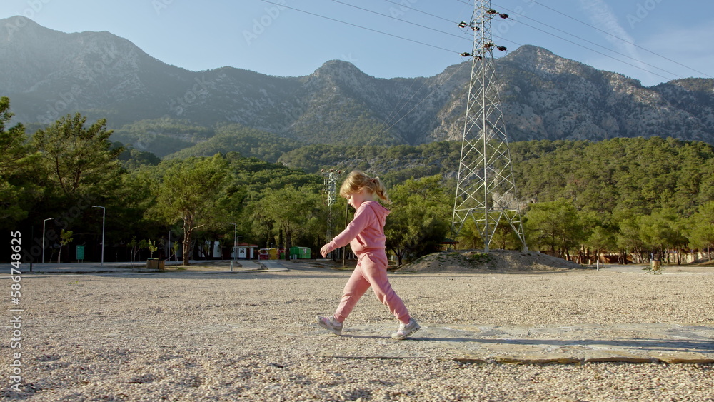 sad upset child in pink tracksuit walk along path with mountains in ...