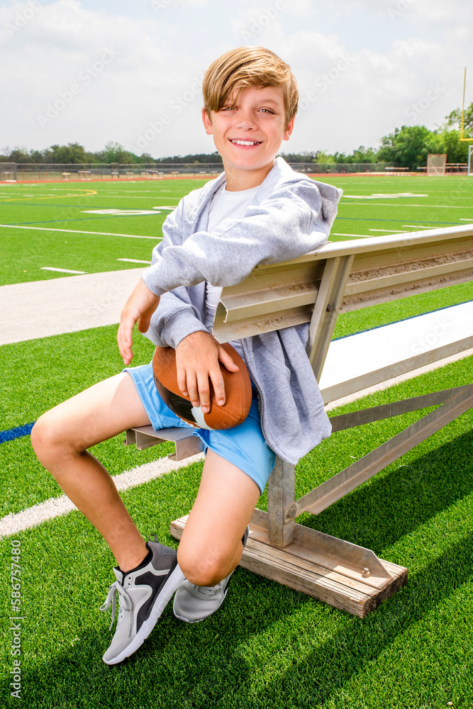 Smiling preteen boy sitting on bench on the sideline of a football ...