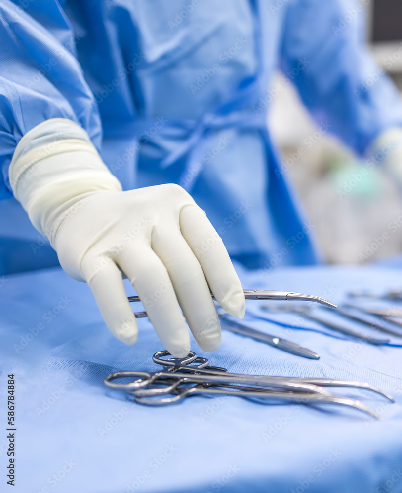 Hand of doctor or surgeon in blue gown pick up surgical clamp ...