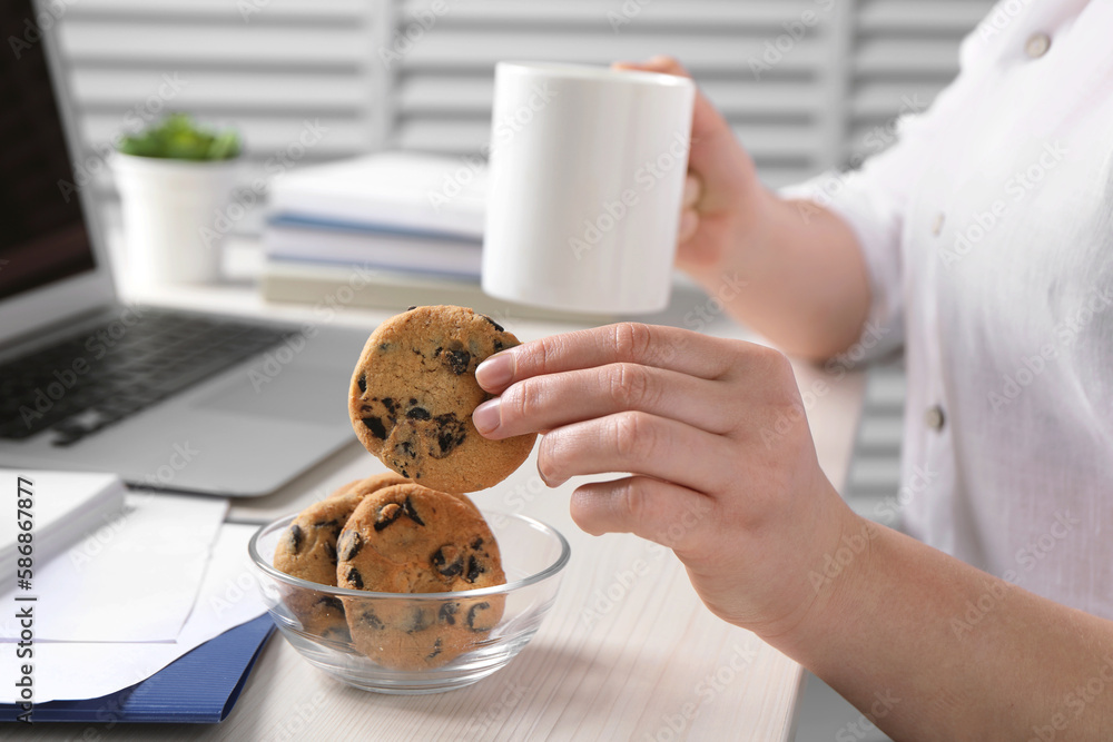 Office worker with cup of drink taking chocolate chip cookie from bowl ...